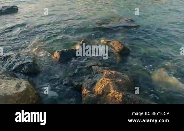 Blue sea waves crash against rocky coastline on a sunny day with ...