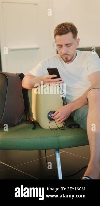 Traveler sits in airport waiting area and connects phone to charging ...