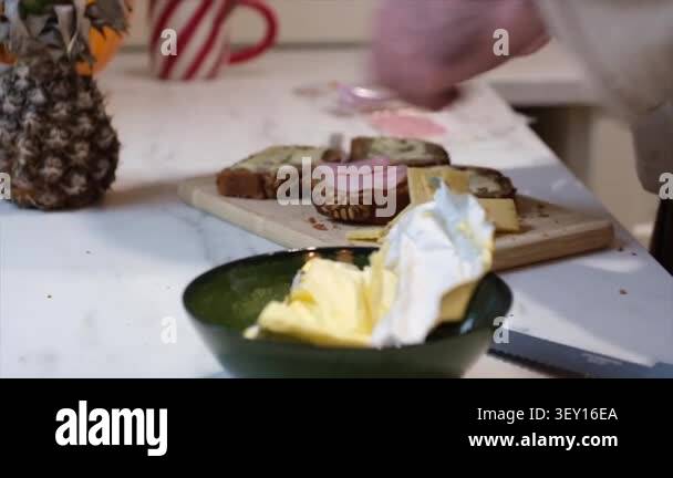 Close up footage of a man placing slices of ham onto buttered seeded ...