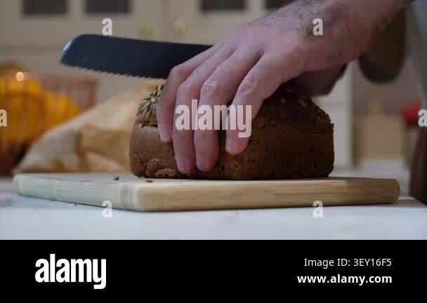 Medium close up footage of a man slicing fresh seeded bread with a ...