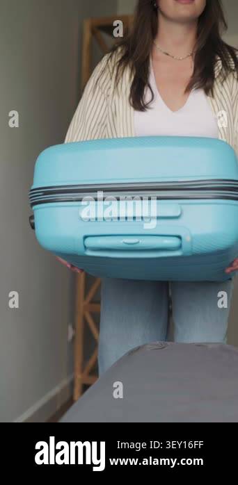 Young woman places blue suitcase on bed and opens it to pack clothes ...