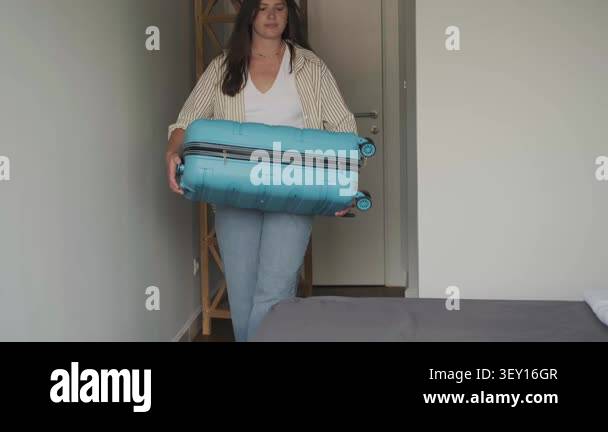 Woman brings blue suitcase into room and places it on bed before trip ...