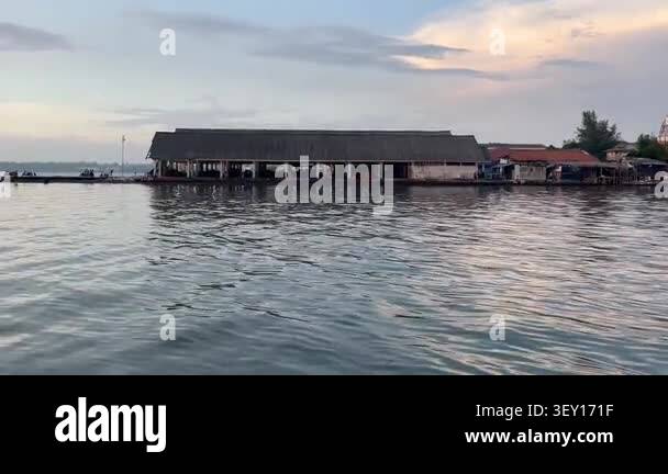 A long, rectangular building with a dark roof floats on calm water ...