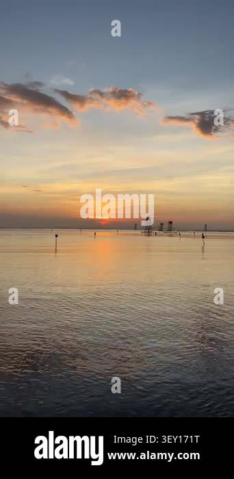 A serene coastal sunset over calm water. The sky displays a stunning ...
