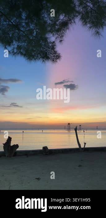 A serene coastal sunset over calm water. The sky displays a stunning ...