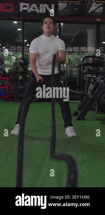 A determined young Asian man is performing an intense battle rope ...