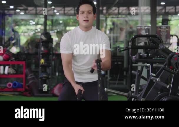 A determined young Asian man is performing an intense battle rope ...