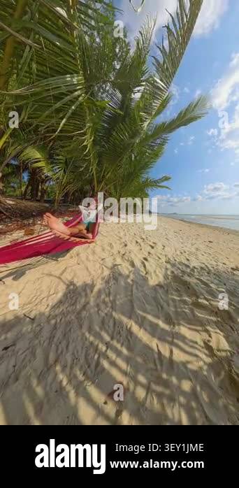 Vertical video. Tropical Coastal Retreat, Man Relaxing in Red Hammock ...