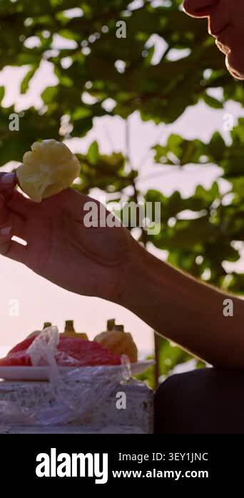Vertical video. Person Eating Fresh Tropical Fruit Near Ocean at Sunset ...