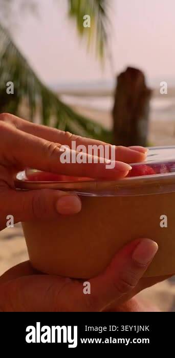 Vertical video. Hand Opening Container with Fresh Cut Fruit on Beach ...