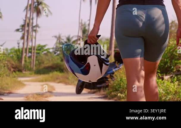 Woman Walking Away Holding Helmet Along Sandy Road Near Scooter in ...