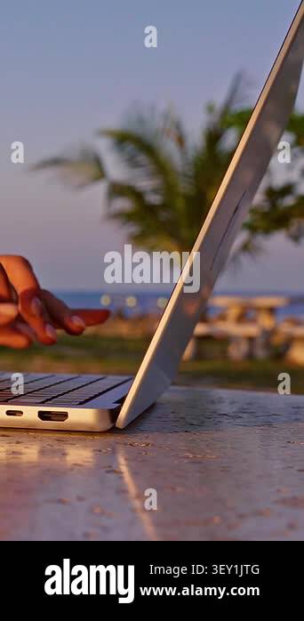 Vertical video. Woman Typing on Laptop at Outdoor Table by Ocean During ...