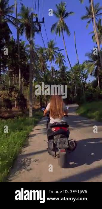 Vertical video. Young Woman Riding Scooter Along Tropical Road ...