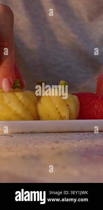 Vertical video. Close Up of Woman Eating Mini Pineapple in Warm Sunset ...