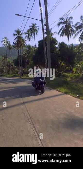 Vertical video. Young Woman Riding Scooter Toward Camera on Tropical ...
