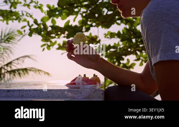 Person Eating Fresh Tropical Fruit Near Ocean at Sunset with Palm Trees ...