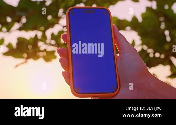 Hand Holding Smartphone with Blank Blue Screen Against Sunset and ...