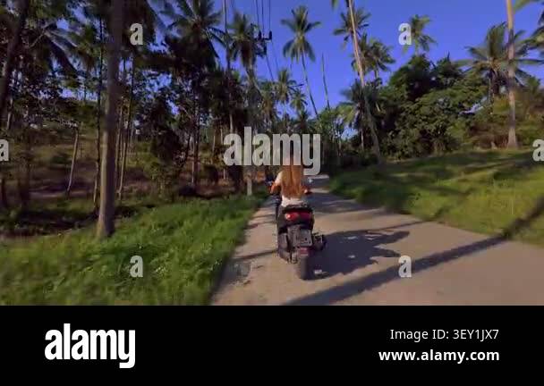 Young Woman Riding Scooter Along Tropical Road Surrounded by Tall Palm ...