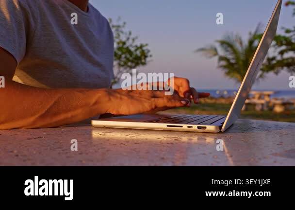 Woman Typing on Laptop at Outdoor Table by Ocean During Sunset with ...