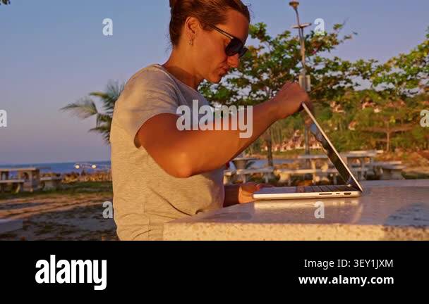 Young Woman Working on Laptop at Seaside During Sunset with Ocean and ...