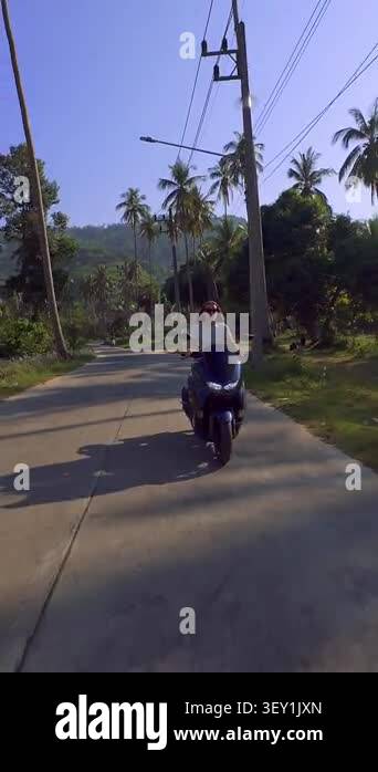 Vertical video. Young Woman Riding Scooter Toward Camera on Tropical ...