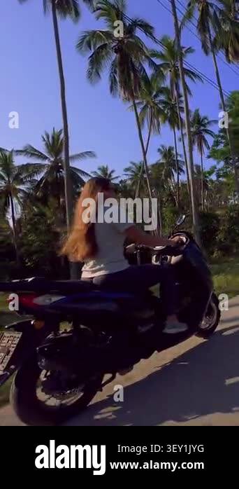 Vertical video. Side View of Young Woman Riding Scooter Along Tropical ...