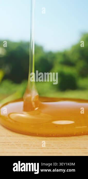 Vertical video. Thin Stream Of Golden Honey Falling Onto Wooden Surface ...