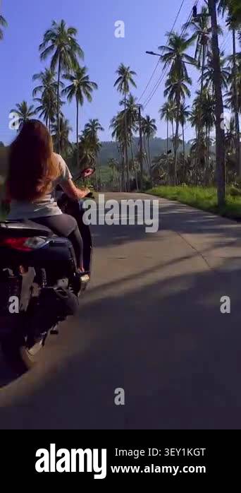 Vertical video. Rear View of Young Woman Riding Scooter on Tropical ...