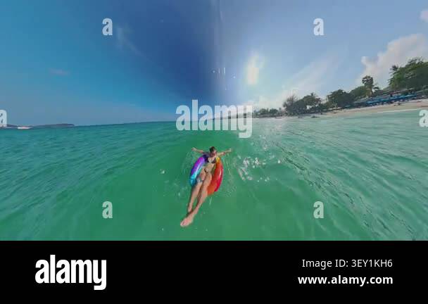Woman Floating On Inflatable Ring In Open Sea With Coastline In ...