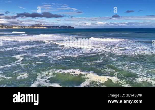 Wide coastal vista with gentle breakers, sunlit water and rhythmic foam ...