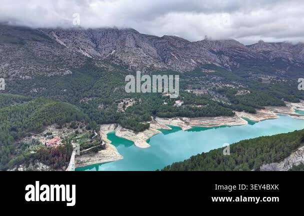 Turquoise reservoir beneath clouded mountain peaks, cinematic drone ...