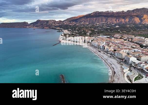Aerial view of turquoise bay with sunlit promenade, mountain backdrop ...