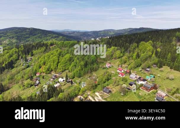 Aerial view dense forest ridge with scattered cabins, winding dirt ...