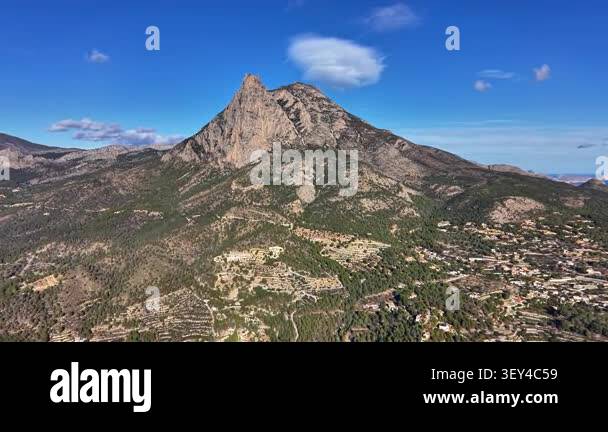 Sunlit jagged peak above rural terraces, crisp blue sky, dramatic rock ...