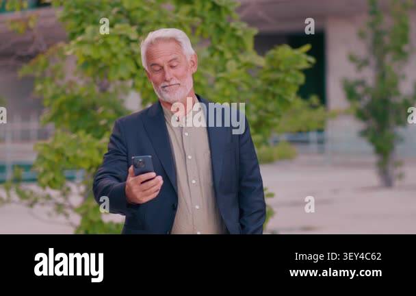 Senior businessman using smartphone while standing near modern office ...