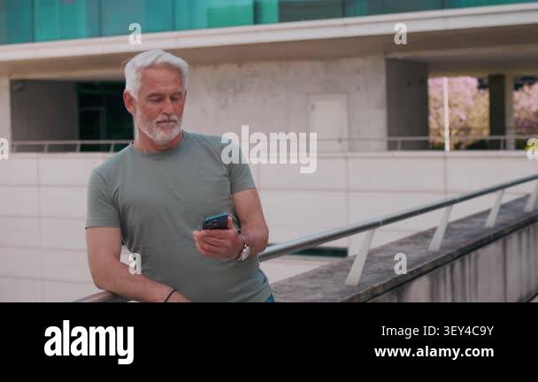 Mature man using smartphone near urban building. He appears relaxed and ...