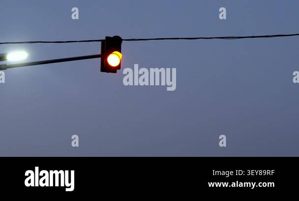 A flashing traffic light against the evening sky at an intersection ...