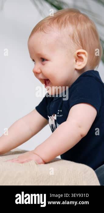 Adorable smiling baby boy stands holding by the sofa. Cute cheerful ...