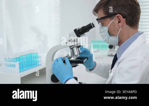 Masked male scientist in lab coat, protective glasses and blue gloves ...