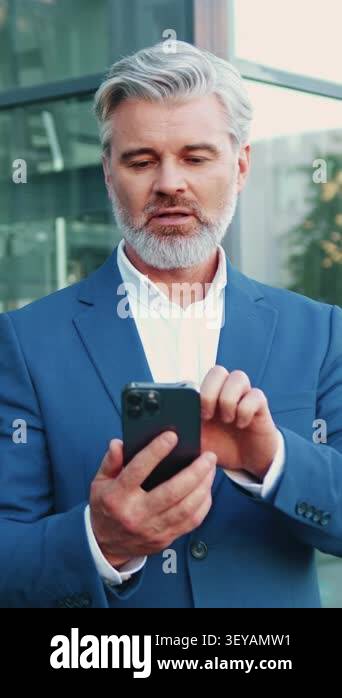 Attractive old man wearing white shirt holding phone and celebrating ...