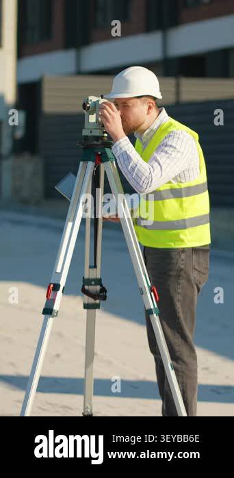 Land surveyor using a theodolite on a tripod for measurements at a ...