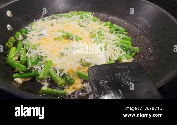 Green asparagus and cheese mixture cooking in a frying pan, spatula ...