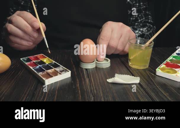 Person engaged in painting an egg with a brush, applying orange color ...