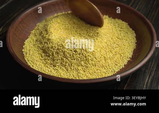 Yellow millet grains are displayed in a wooden bowl, with a wooden ...