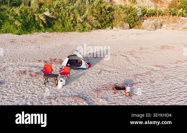 Aerial footage of simple seaside setup with tent and chairs in warm ...