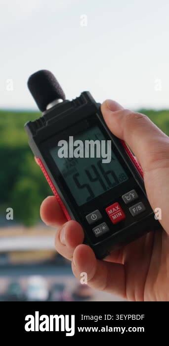 A hand holds a digital sound level meter displaying decibels against a ...