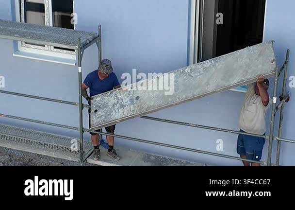 Two men on a construction site are carefully handling large metal ...