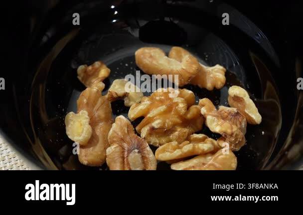 Walnut kernels rotate inside a glossy black bowl, showing their ridges ...