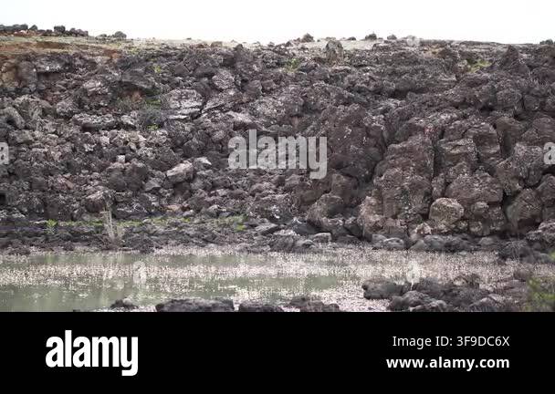 Basalt lava plain with calm lake water and dark volcanic rock reveals a ...