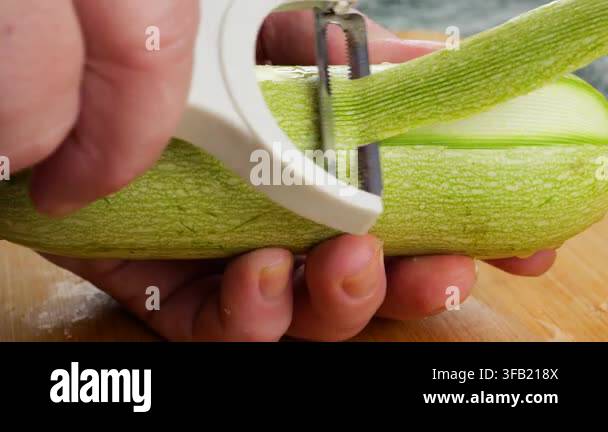 A close-up shot captures a chef using a white vegetable peeler with a ...